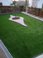Um jardim ajardinado com grama sintética, uma pequena árvore e uma borda de cascalho branco.