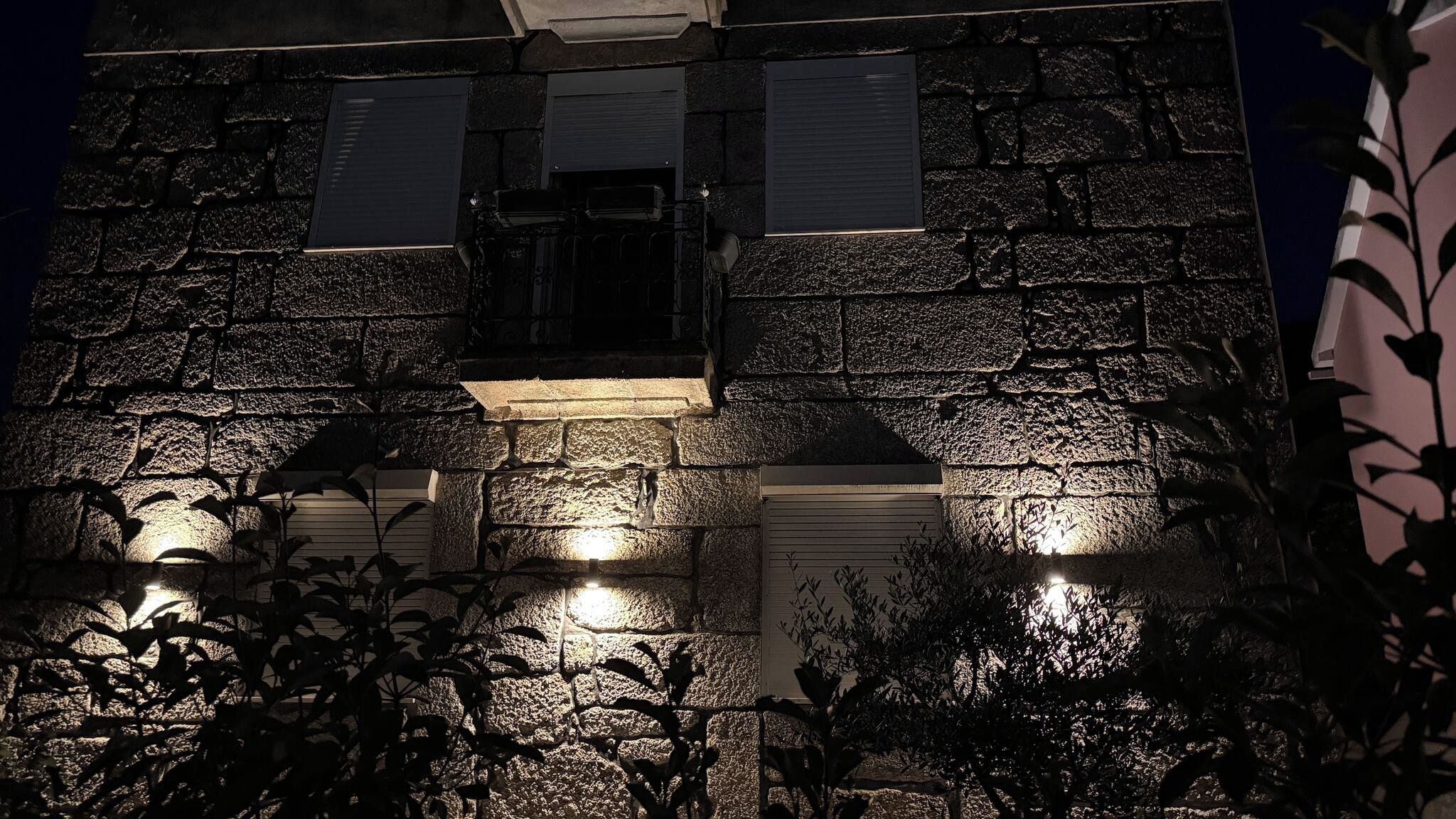 Um edifício de pedra com varanda e duas janelas iluminadas.