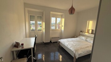 Quarto com cama, escrivaninha e cadeira. Possui duas janelas e um radiador.