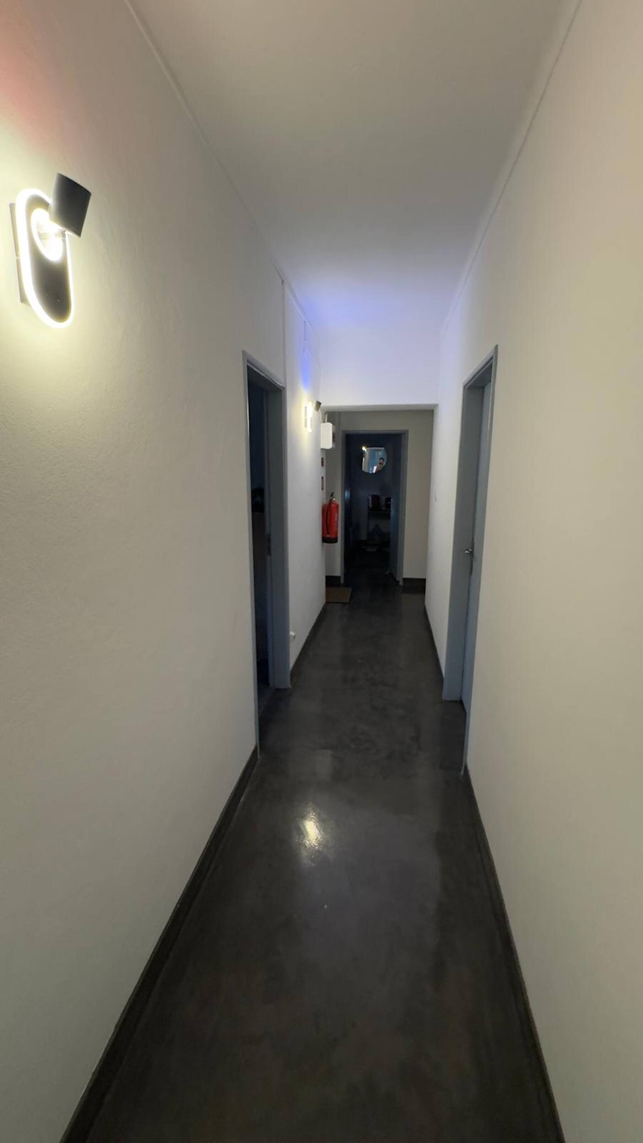 Um corredor com luminárias nas paredes, um extintor de incêndio e uma porta no final.