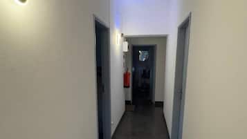 Um corredor com luminárias nas paredes, um extintor de incêndio e uma porta no final.