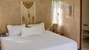 Quarto com uma cama grande, uma mesa de cabeceira com abajur, um ornamento na parede e uma janela com cortinas.
