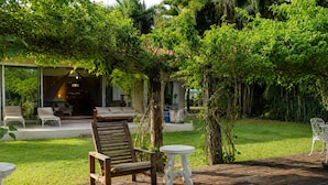 Um deck de madeira com piscina, espreguiçadeiras e uma área de estar coberta, com vista para o verde.