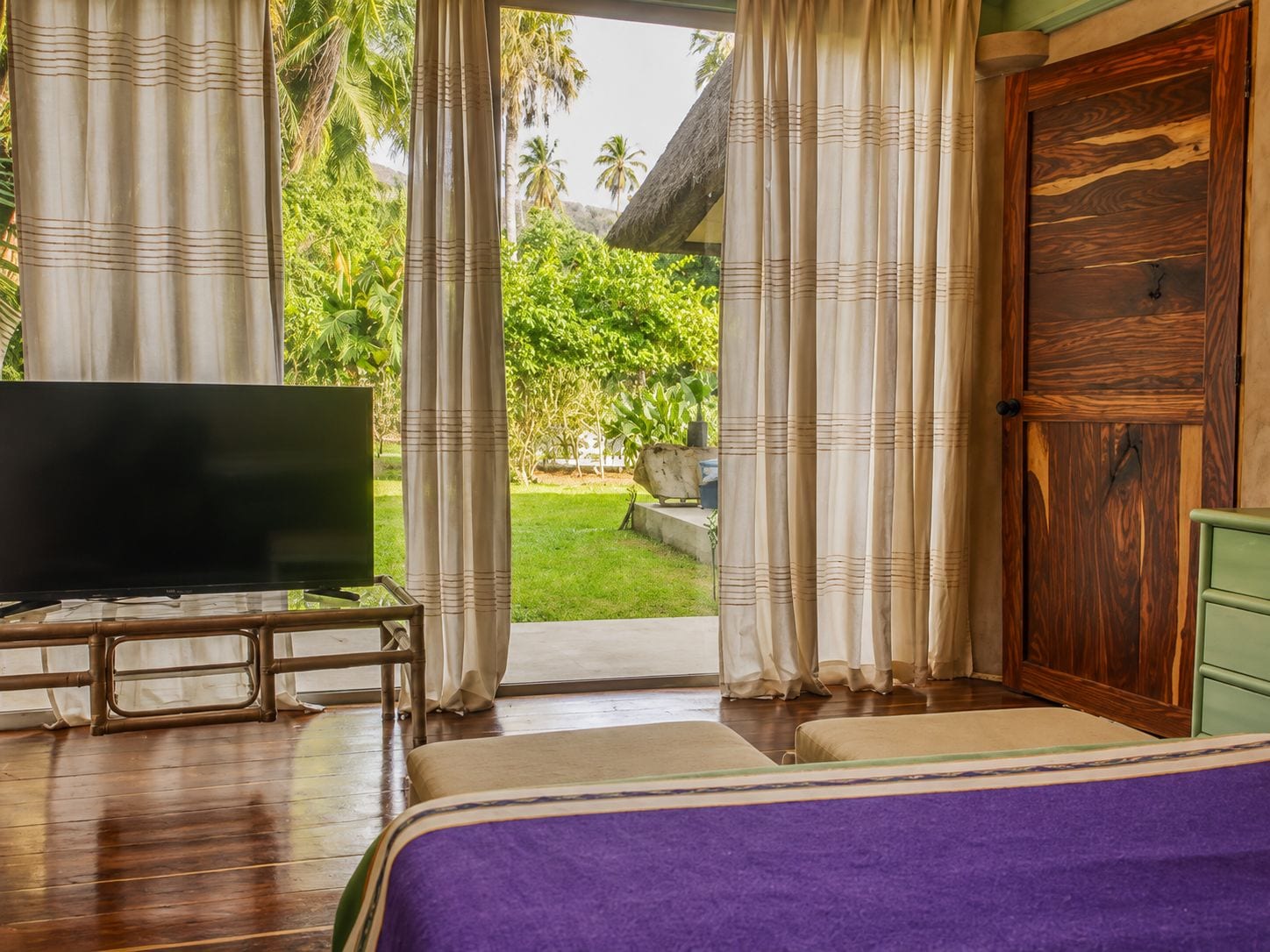 Quarto com televisão, cama e vista para o jardim.