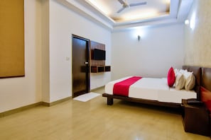 Quarto de hotel com cama, porta, ventilador de teto e televisão de tela plana na parede.