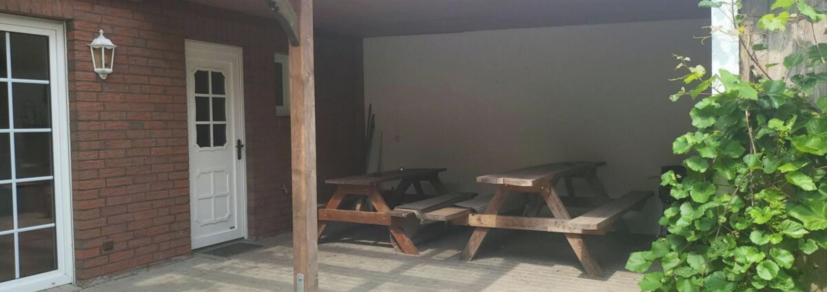 Edifício de tijolos com porta e janelas brancas, um banco de madeira e um arandelador.