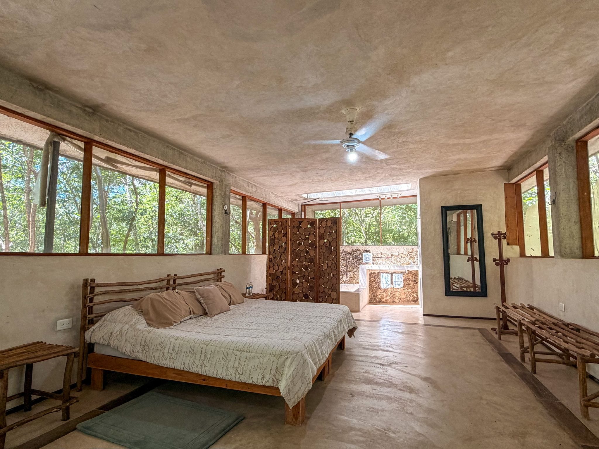 Quarto com cama, ventilador de teto e vista para o exterior.