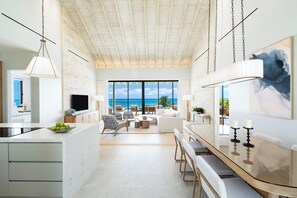 Ampla sala de estar com uma grande janela com vista para o oceano, cozinha com design moderno e área de jantar com balcão.