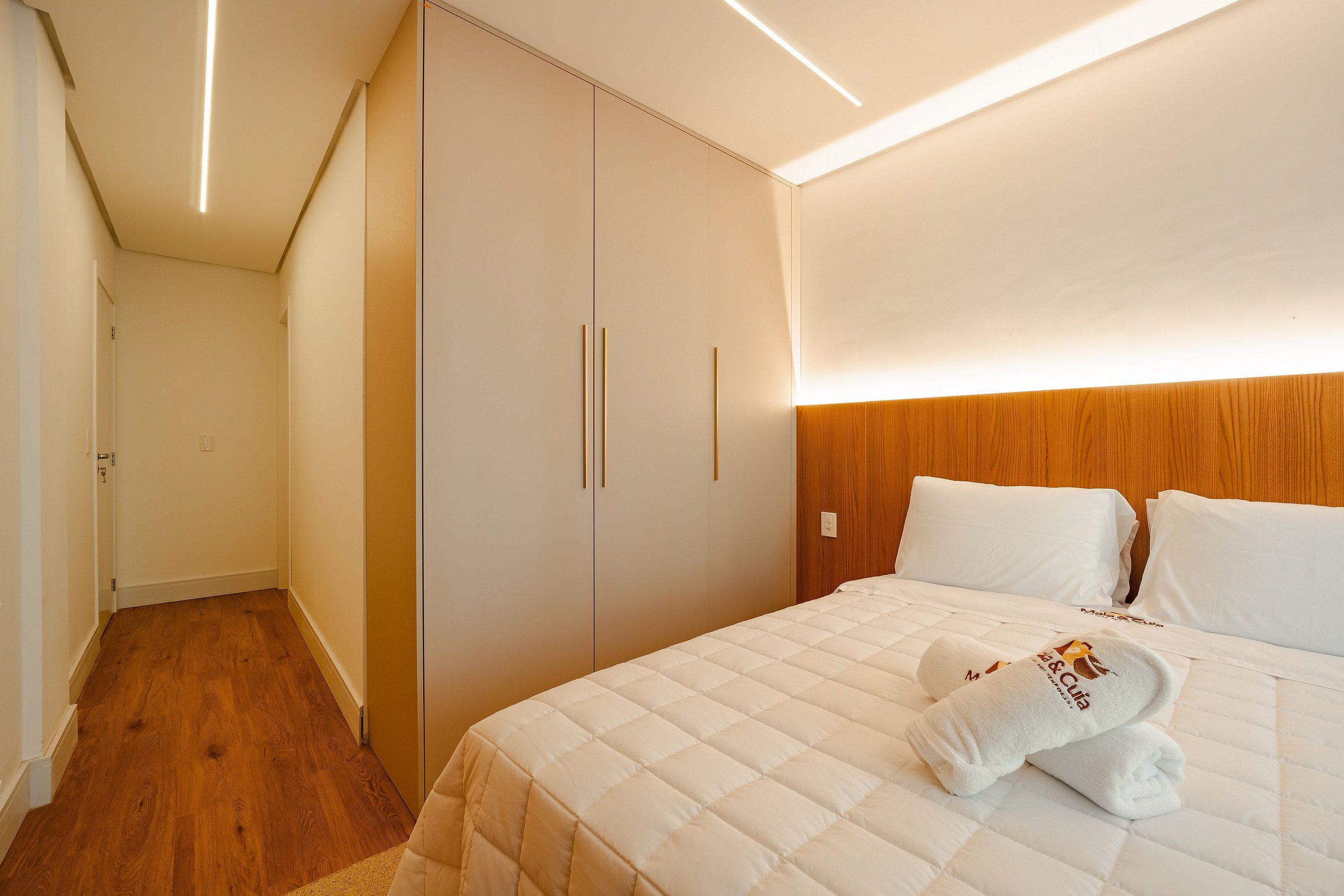 Quarto de hotel com cama, cabeceira de madeira e guarda-roupa.