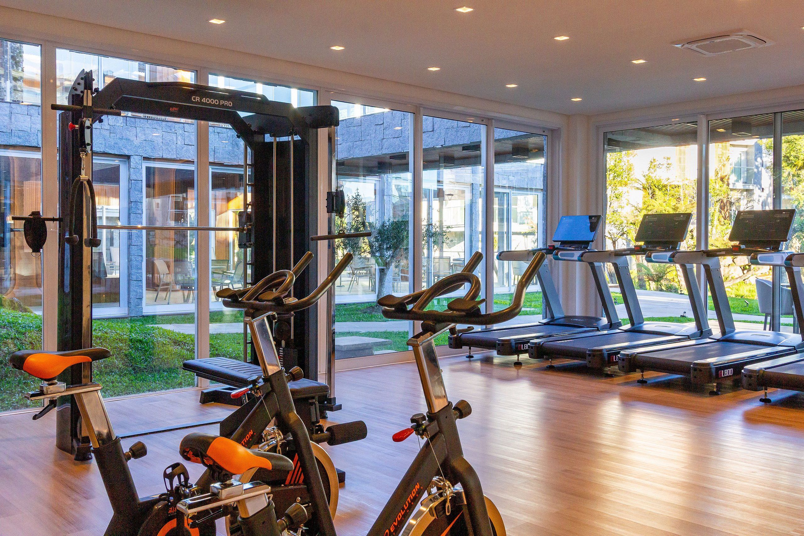 Academia com equipamento de exercícios, janelas amplas e vista para o exterior.