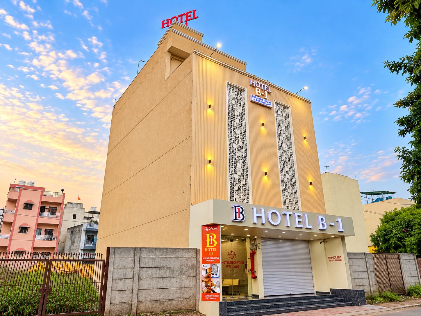 Hotel com um grande letreiro 'HOTEL B-1', área de recepção e entrada com portão.