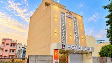 Hotel com um grande letreiro 'HOTEL B-1', área de recepção e entrada com portão.