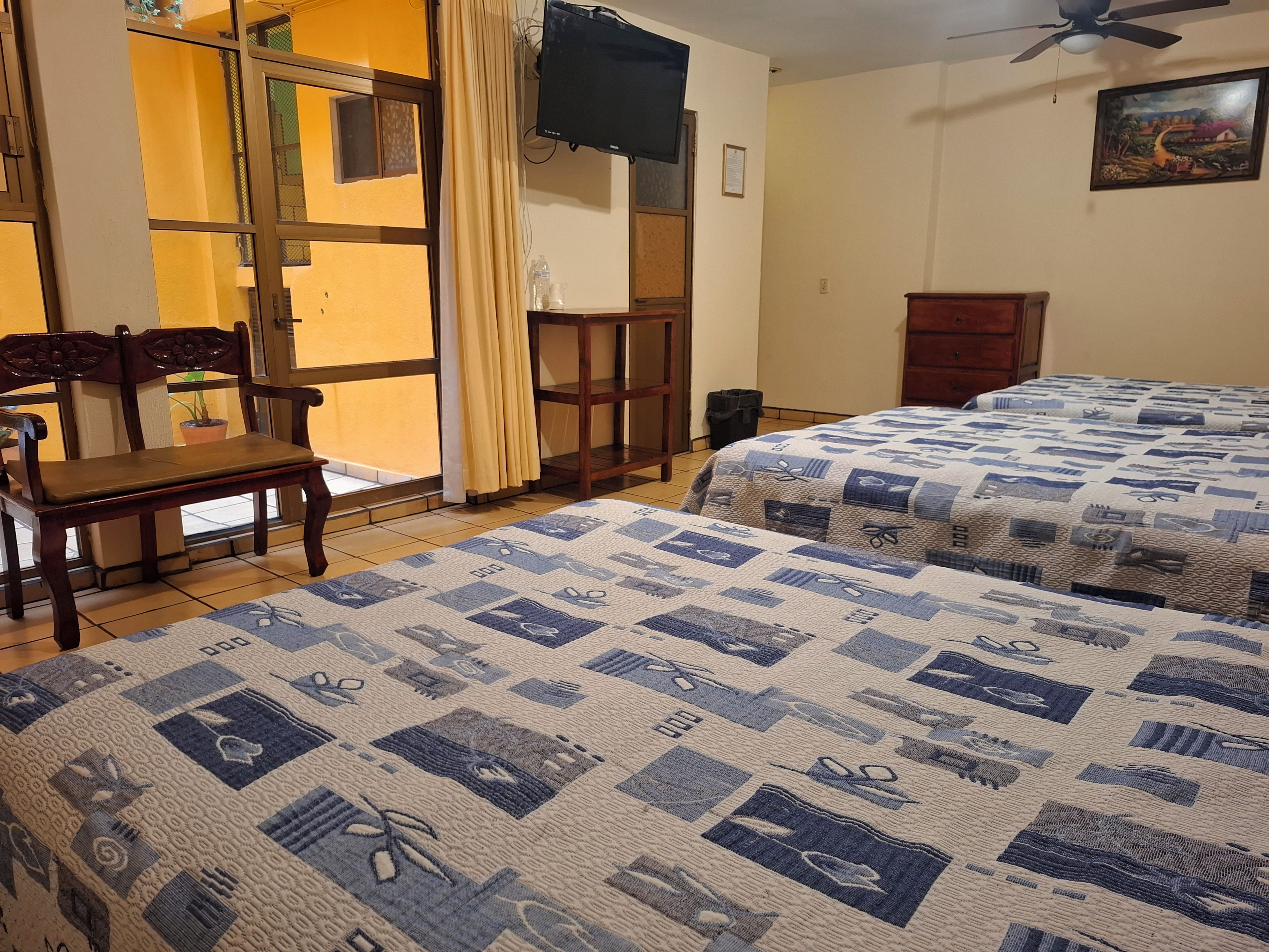 Quarto de hotel com duas camas, uma cadeira de madeira, uma televisão e um quadro na parede.