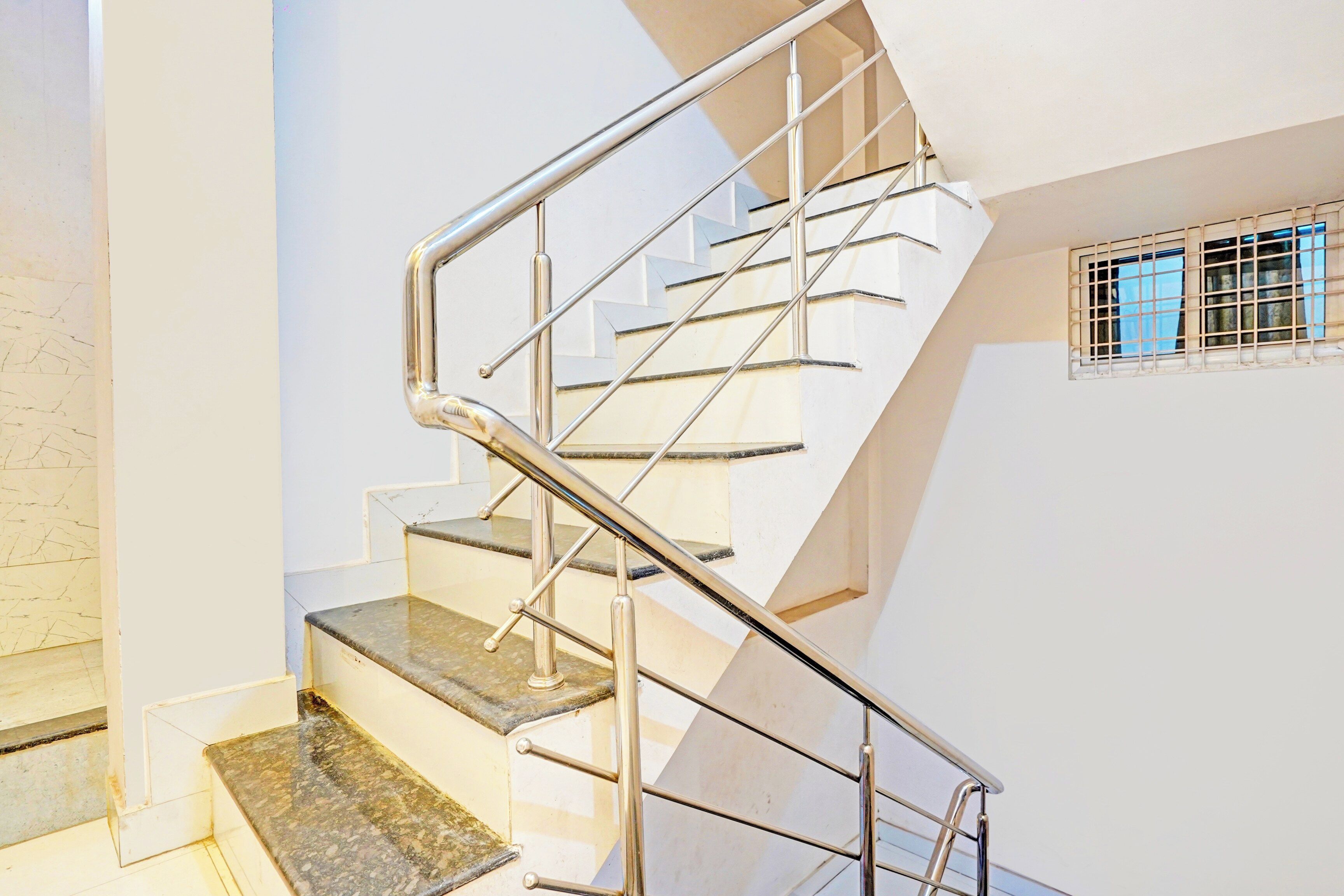 Escadaria em espiral com corrimão de metal e uma janela com grades.