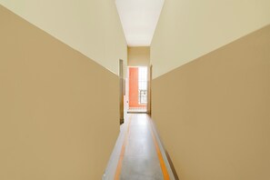 Um corredor com paredes bege e chão de azulejos, que leva a uma porta aberta com janela.