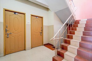 Escadaria com corrimão, que leva a um patamar com duas portas de madeira, cada uma com fechadura e placa de identificação.