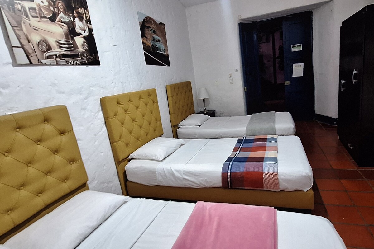 Quarto de hotel com três camas, um guarda-roupa e uma porta.