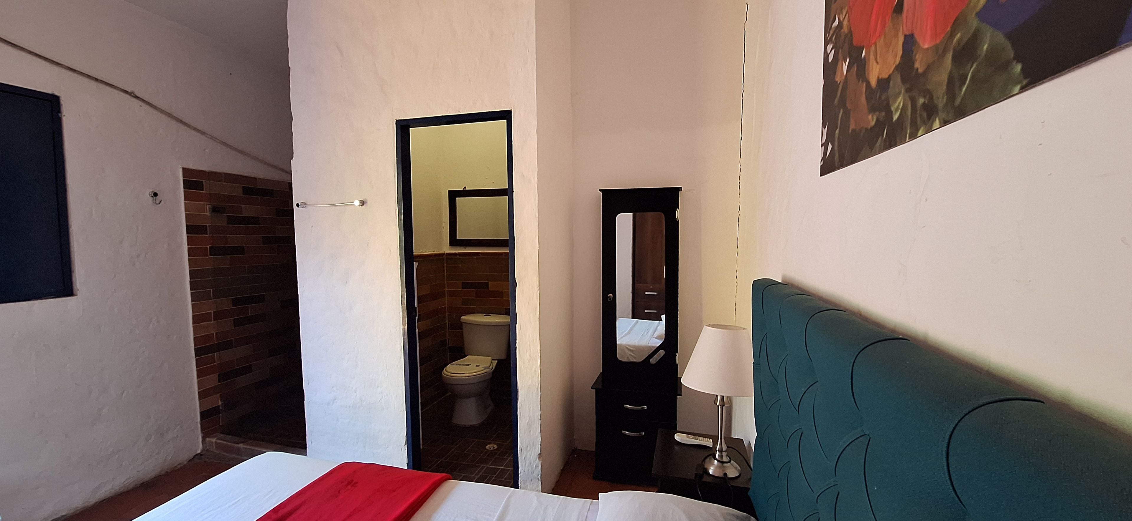 Quarto de hotel com cama, mesa de cabeceira, espelho, quadro na parede e vista para o banheiro.