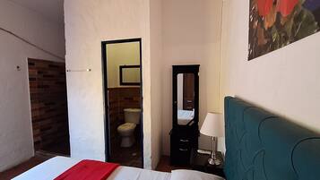 Quarto de hotel com cama, mesa de cabeceira, espelho, quadro na parede e vista para o banheiro.