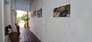 Um corredor com chão de tijolos, paredes brancas e diversas obras de arte emolduradas.