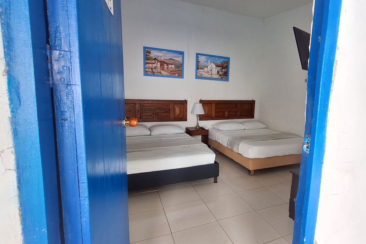 Quarto com duas camas, uma mesinha de cabeceira e duas pinturas penduradas na parede.