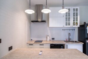 Cozinha moderna com armários brancos, exaustor de aço inoxidável, iluminação pendente e máquina de lavar louça embutida.