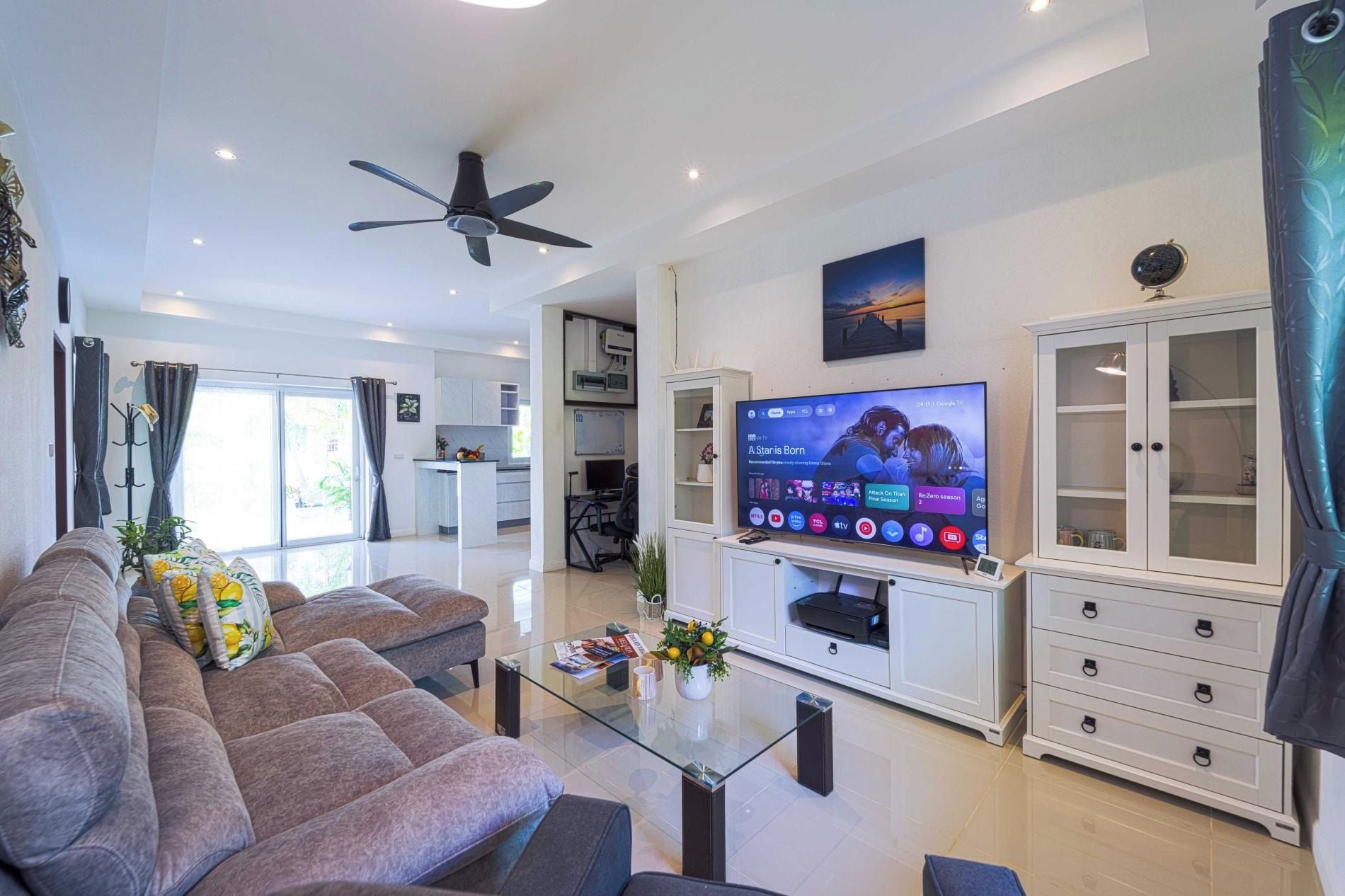 Uma sala de estar moderna com televisão de tela plana, ventilador de teto e mesa de centro de vidro.