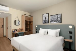 Quarto de hotel com uma cama grande, escrivaninha, cadeira, guarda-roupa e duas imagens emolduradas na parede.