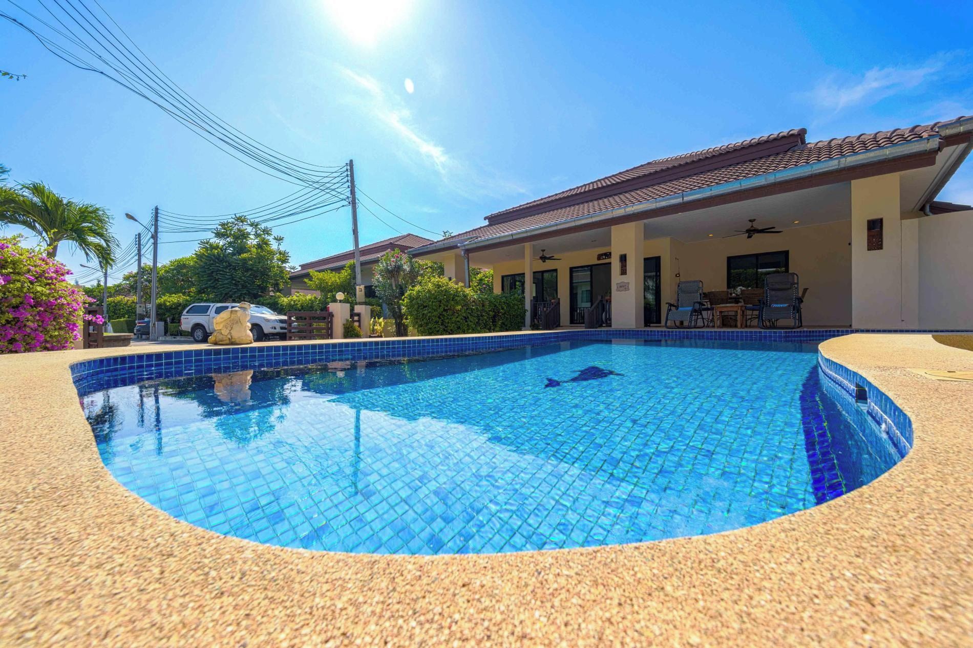Piscina com borda azulejada, rodeada por um espaço coberto com móveis de exterior.