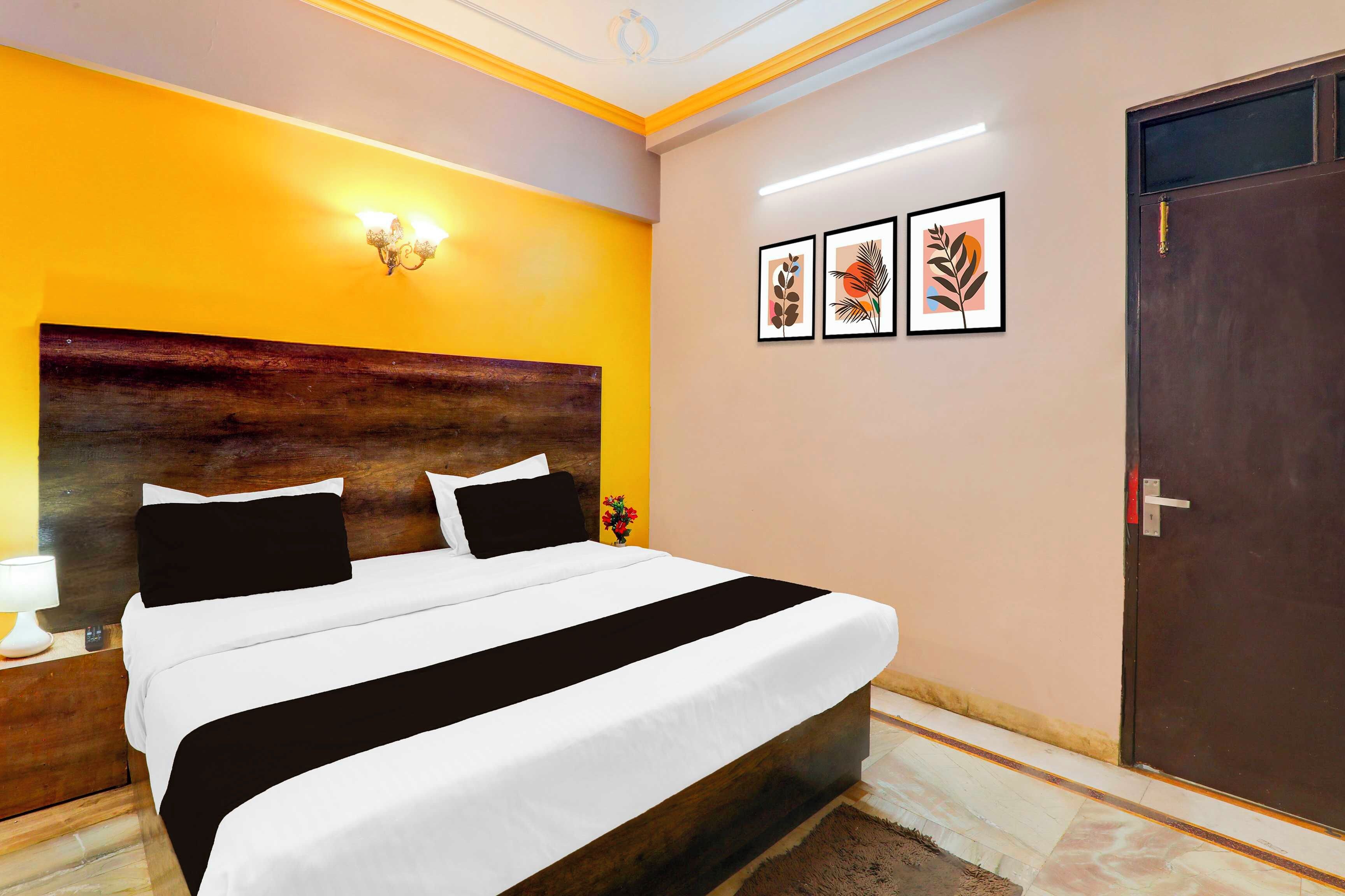 Quarto de hotel com uma cama grande, cabeceira de madeira, mesa de cabeceira com abajur e uma porta.
