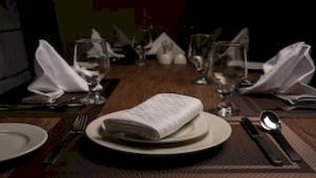 Mesa de jantar posta com pratos, copos, talheres e guardanapo dobrado.