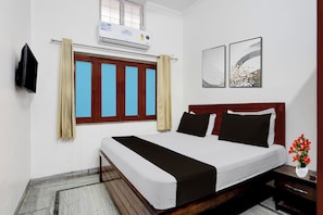 Quarto de hotel com cama, mesa de cabeceira, um vaso com flores, janela com cortinas e duas obras de arte nas paredes.