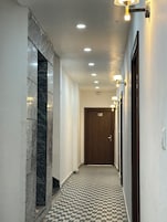 Um corredor com piso xadrez, parede de mármore, iluminação embutida no teto e uma porta com o número 101.