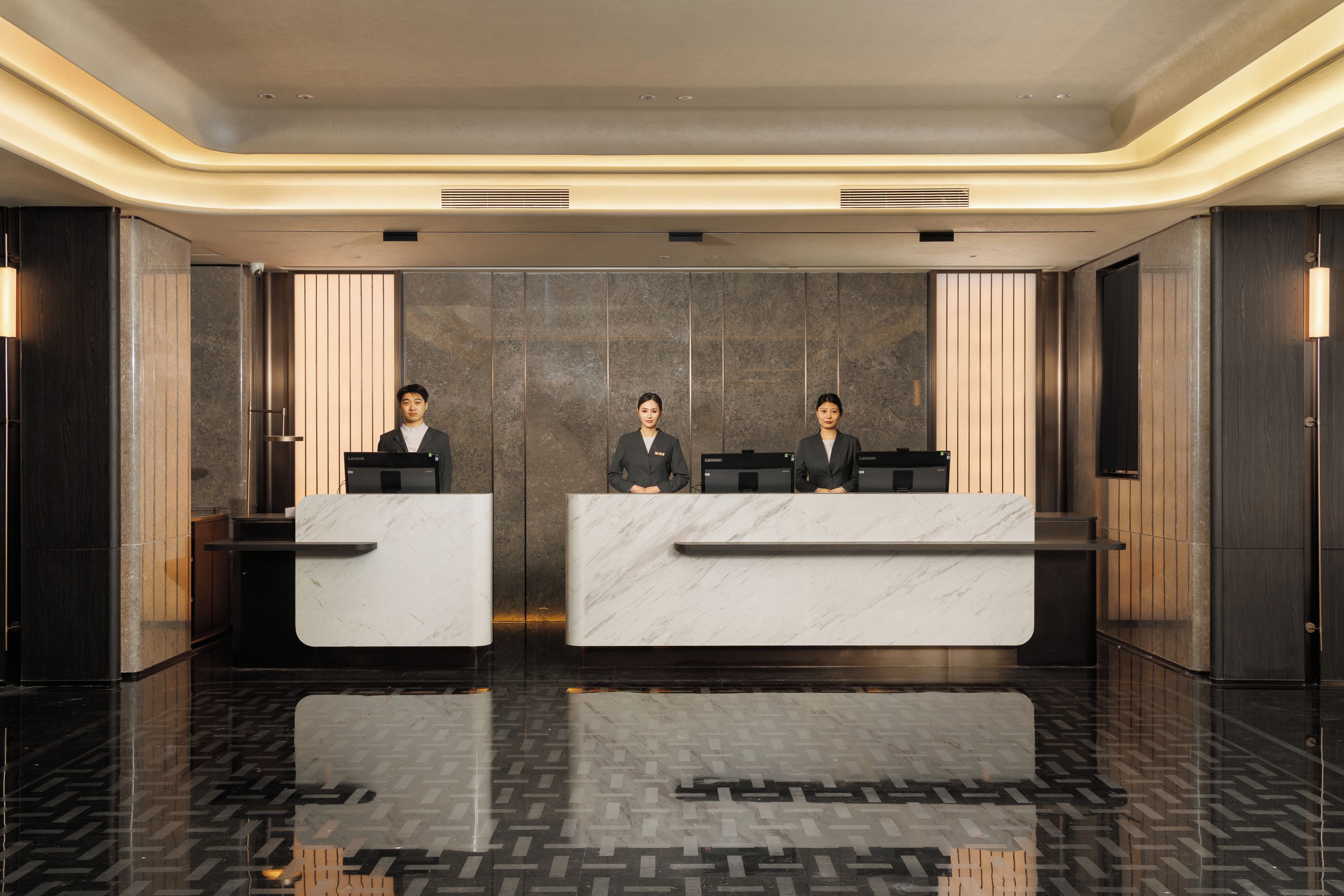 Uma área de recepção com dois recepcionistas em balcões de mármore, design de interiores moderno e piso lustroso.