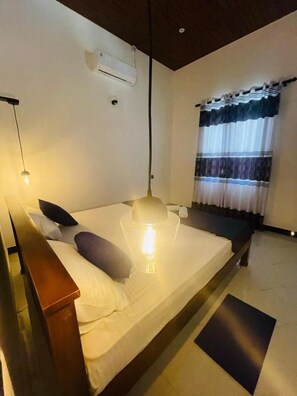 Uma cama de solteiro com cabeceira de madeira, luminária de cabeceira e janela com cortinas.