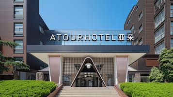 Entrada moderna de hotel com céu claro, uma placa com o texto 'ATOURHOTEL' e uma escadaria que leva à entrada.