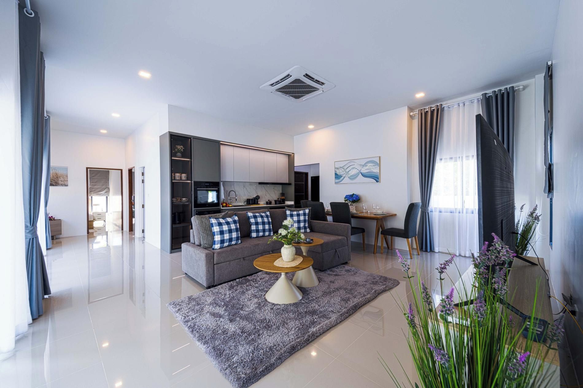 Uma sala de estar moderna com um sofá cinzento, uma mesa de centro e um espaço de jantar com uma mesa pequena e cadeiras.