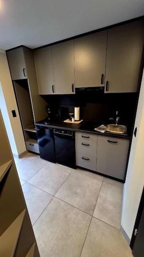 Cozinha compacta com armários escuros, lava-louças e pia.