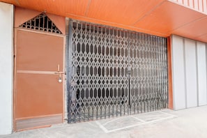 Um portão de metal com design em padrão de losangos, uma porta marrom com fechadura e um chão ladrilhado.