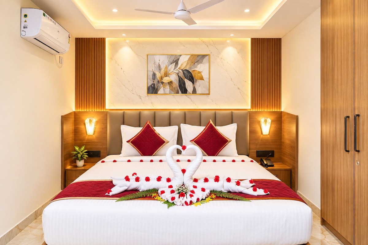 Quarto de hotel com uma cama grande, duas mesas de cabeceira, ar condicionado fixado na parede, ventoinha no teto e um guarda-roupa de madeira.