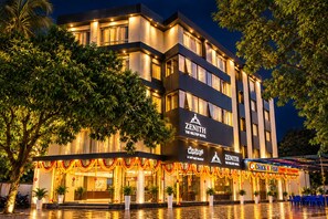 Um hotel de vários andares com fachada moderna, um restaurante visível chamado 'Chick N Fish Family Restaurant' e uma área de entrada bem iluminada.