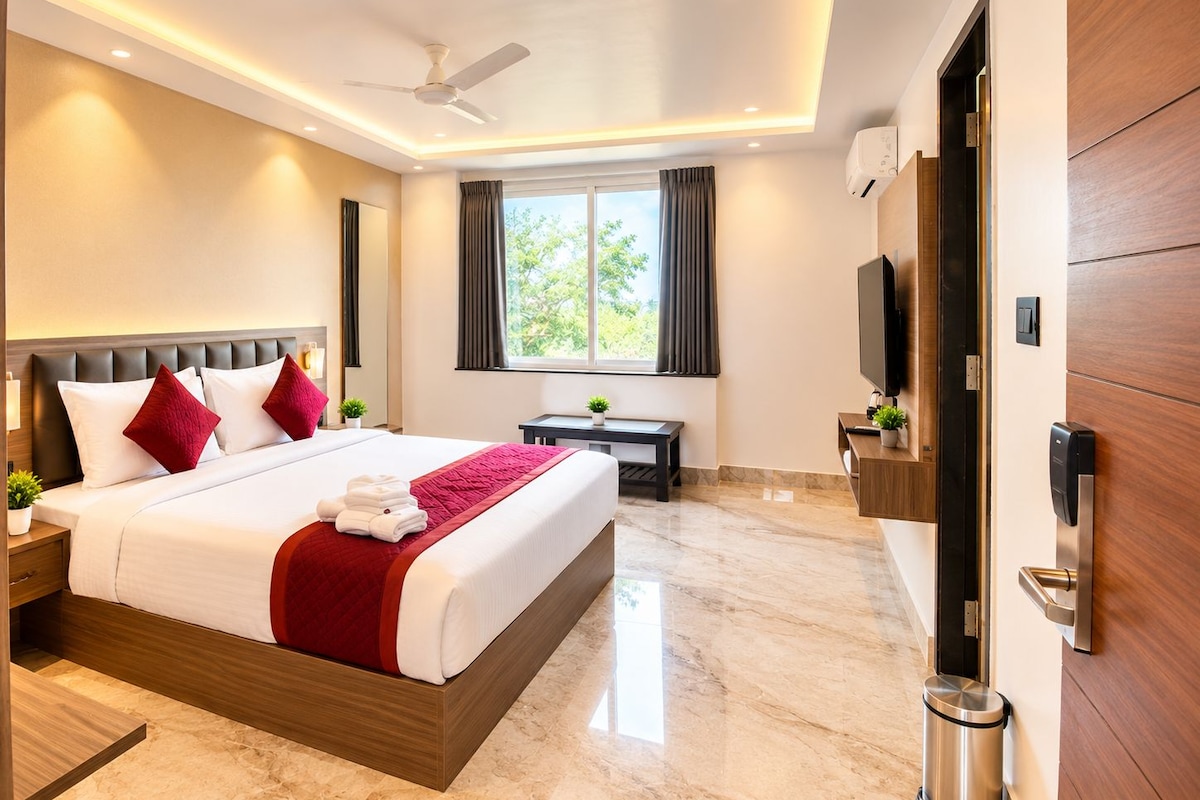 Quarto de hotel com cama, escrivaninha, televisão e janela com cortinas.