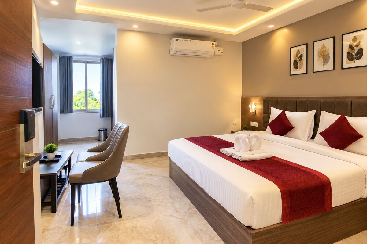 Quarto de hotel com uma cama, uma escrivaninha, uma cadeira, uma televisão e uma janela.