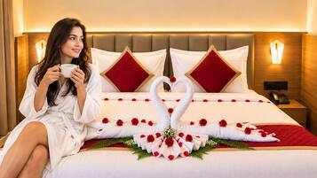Quarto de hotel com cama decorada com cisne feito de rosas e tecido branco, luminária de cabeceira e telefone na mesa de apoio.