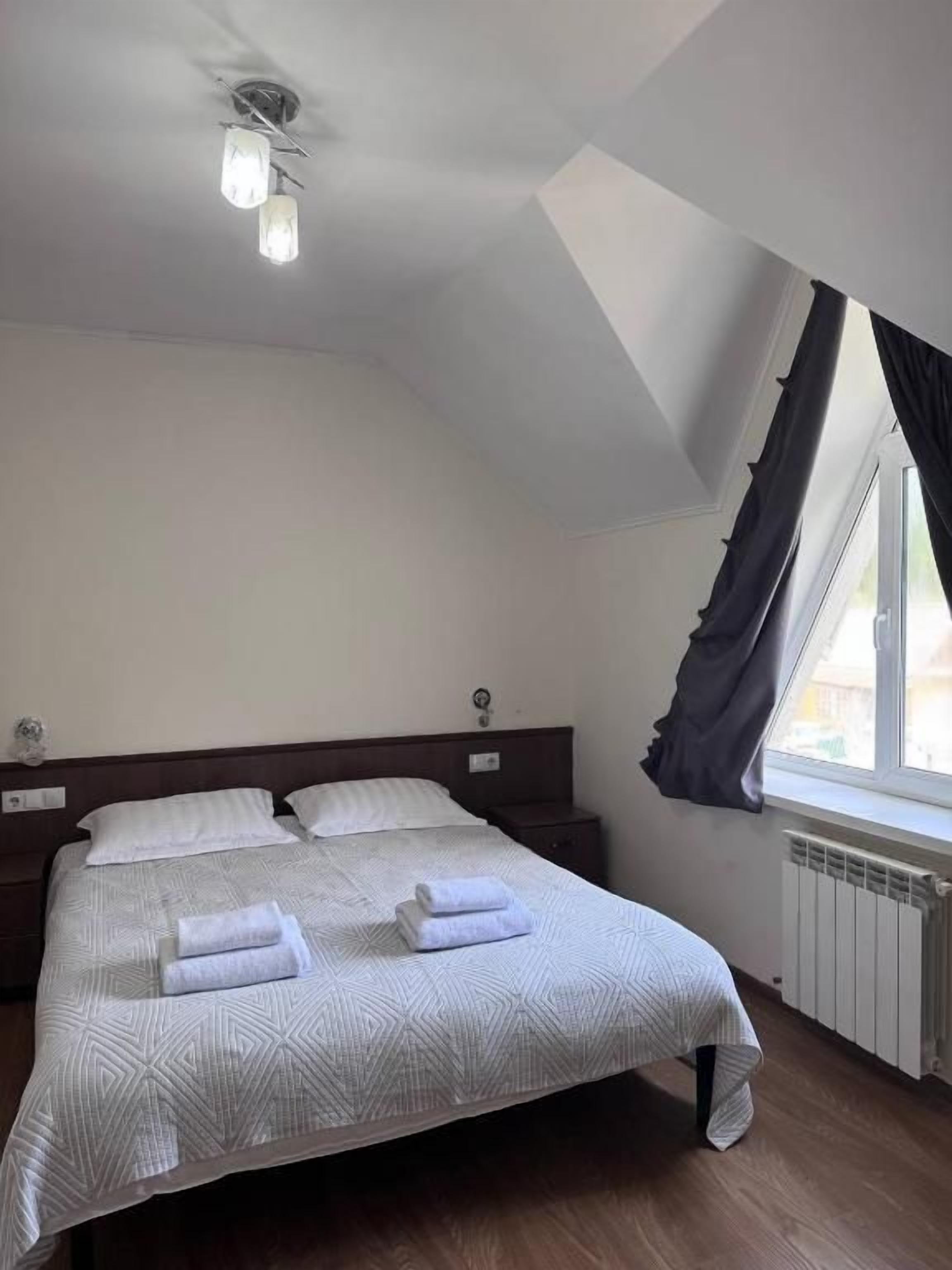 Quarto com cama, janela com cortinas, radiador e luminária no teto.