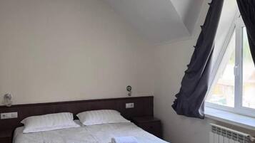Quarto com cama, janela com cortinas, radiador e luminária no teto.