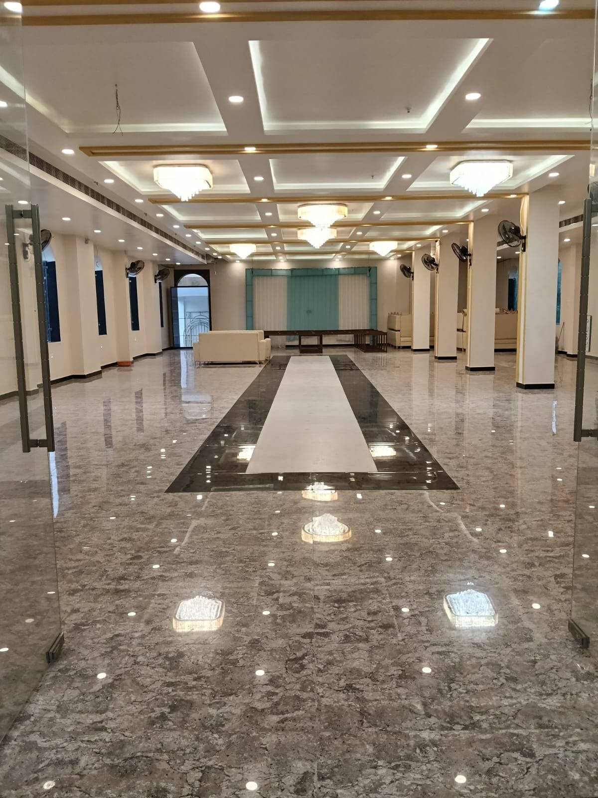 Um amplo hall de hotel com piso de mármore, área de estar central e diversas luminárias no teto.