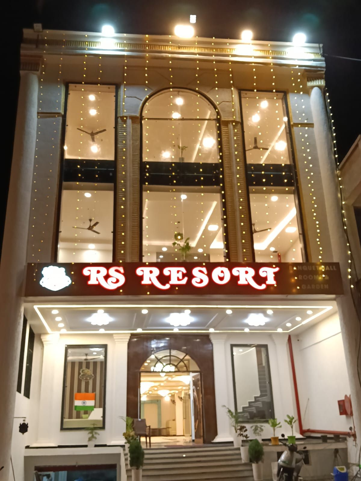 Entrada de um hotel com uma placa indicando 'RS RESORT' e uma bandeira da Índia.