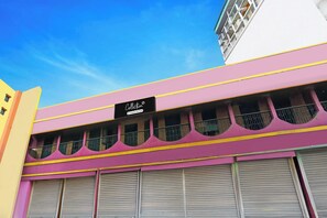 Um edifício com fachada rosa, uma placa preta com texto branco e persianas fechadas.