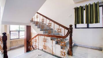 Escadaria com grades de metal decorativas e corrimão de madeira, subindo para um andar superior.